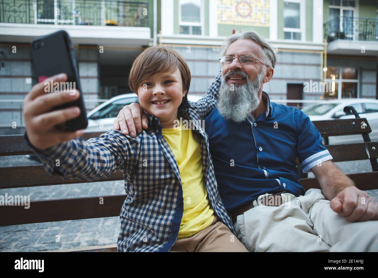 Cheerful young boy taking a selfie with his grandpa on his smart phone ...