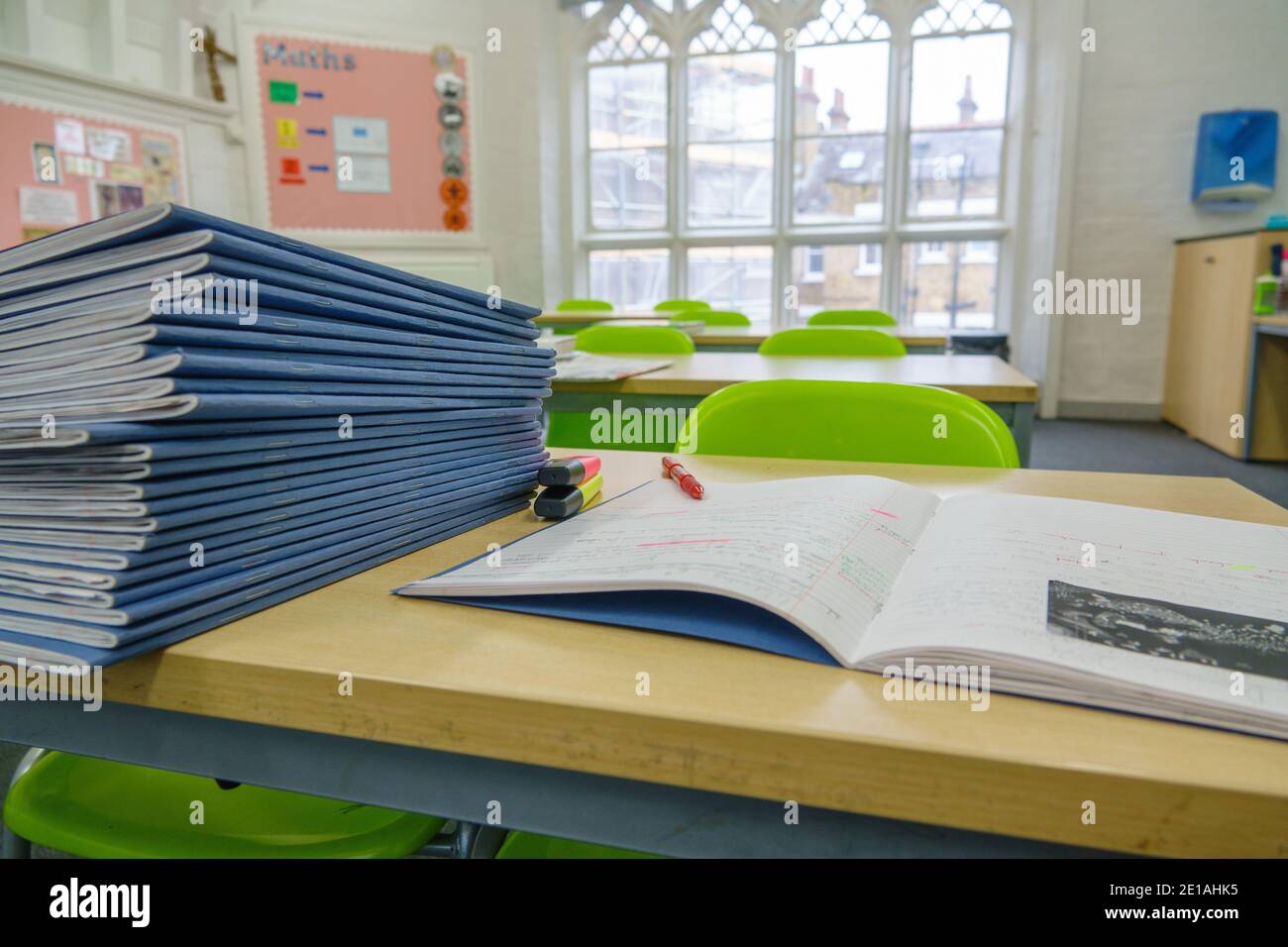 Pile of school books, on a desk, that a teacher is marking, in an empty ...