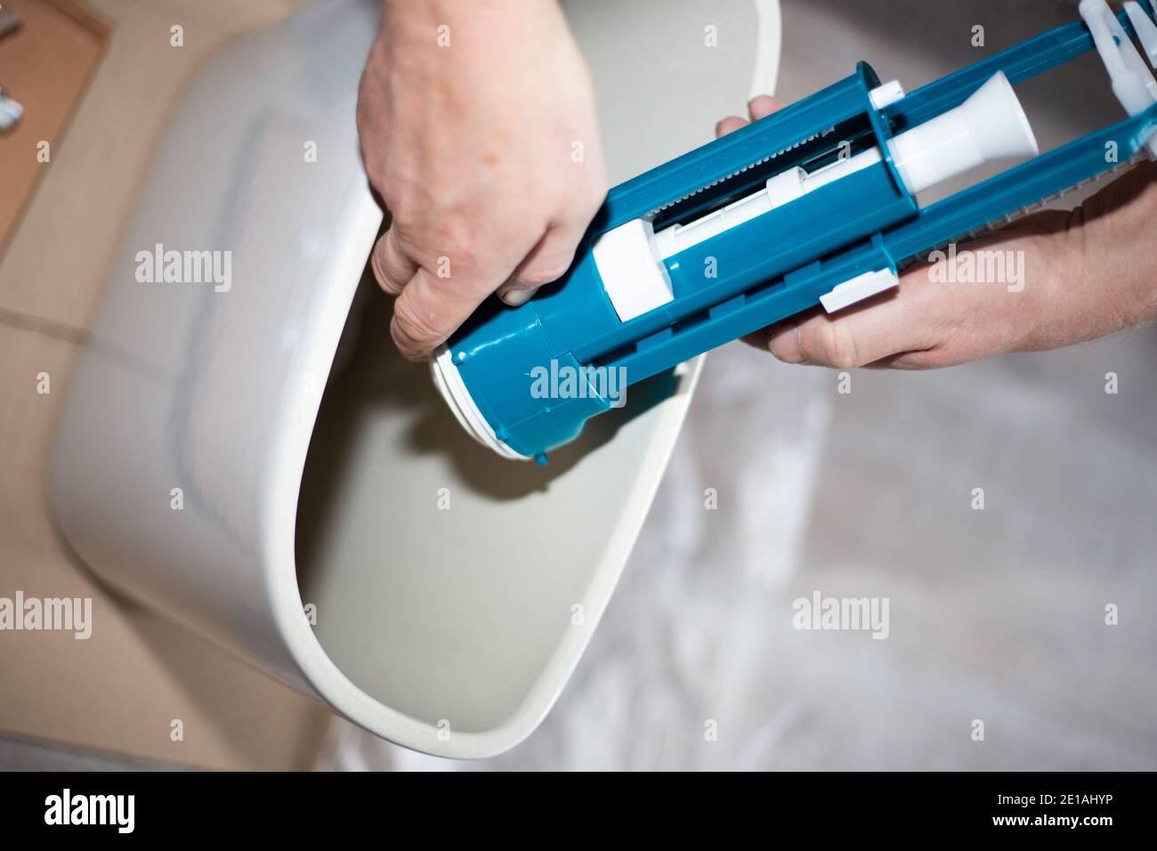 A plumber installs a water pump in a ceramic toilet cistern. Drain ...