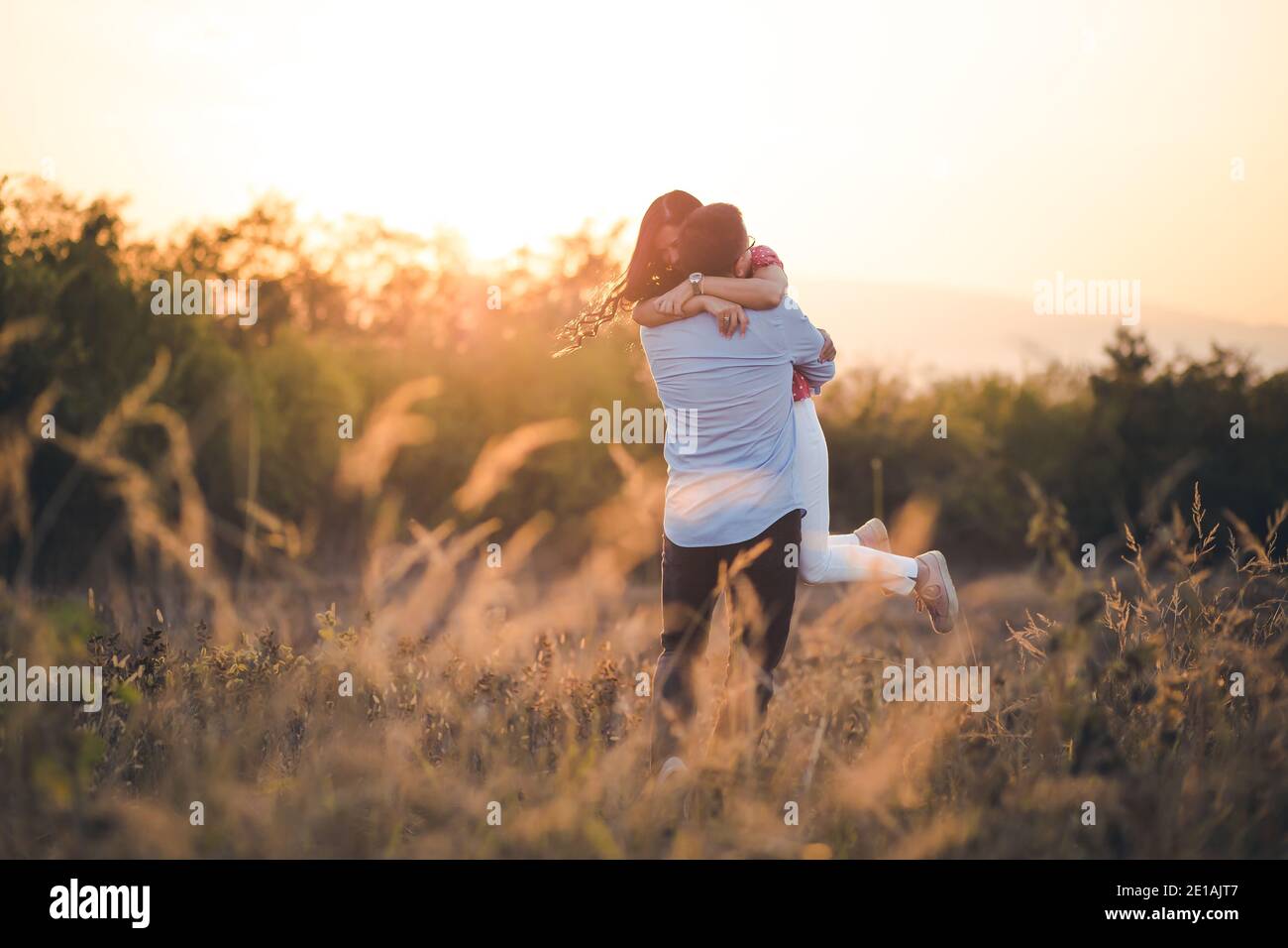 Outdoor portrait of young couple, boyfriend lifts his girlfriend in air ...