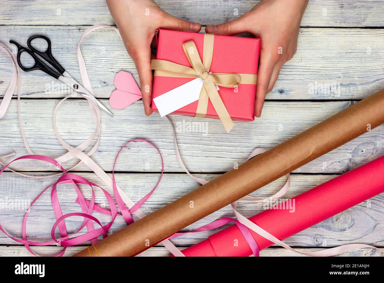 Female hands are preparing a gift wrapped in pink paper. Gift wrapping ...