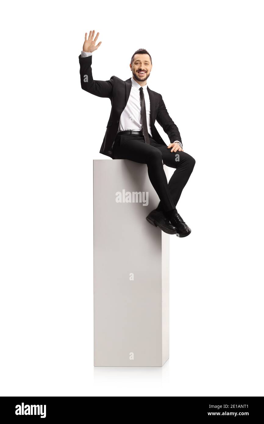 Businessman sitting on a tall white column and waving at camera ...