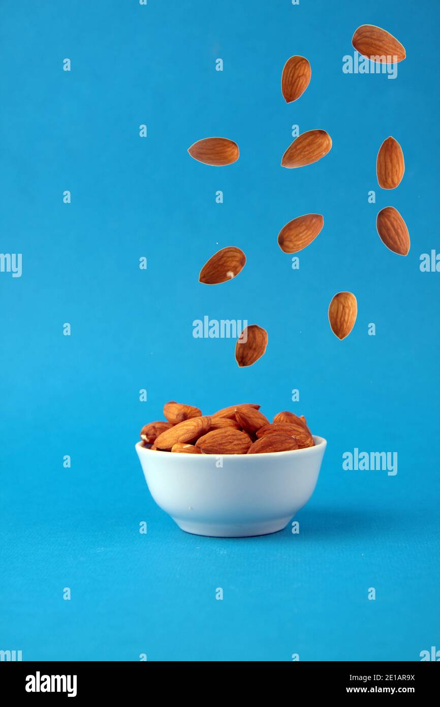 almond pouring into white bowl against blue background. Concept of ...