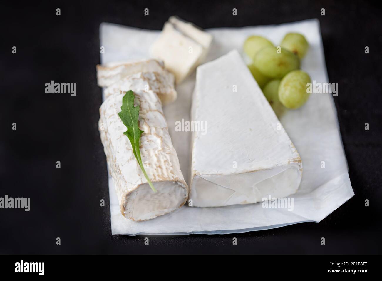 White goat cheese wih green grape on a black background. Fresh goat ...