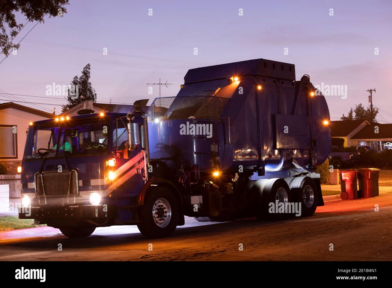 A night time collection of trash by a garbage truck in a suburban ...