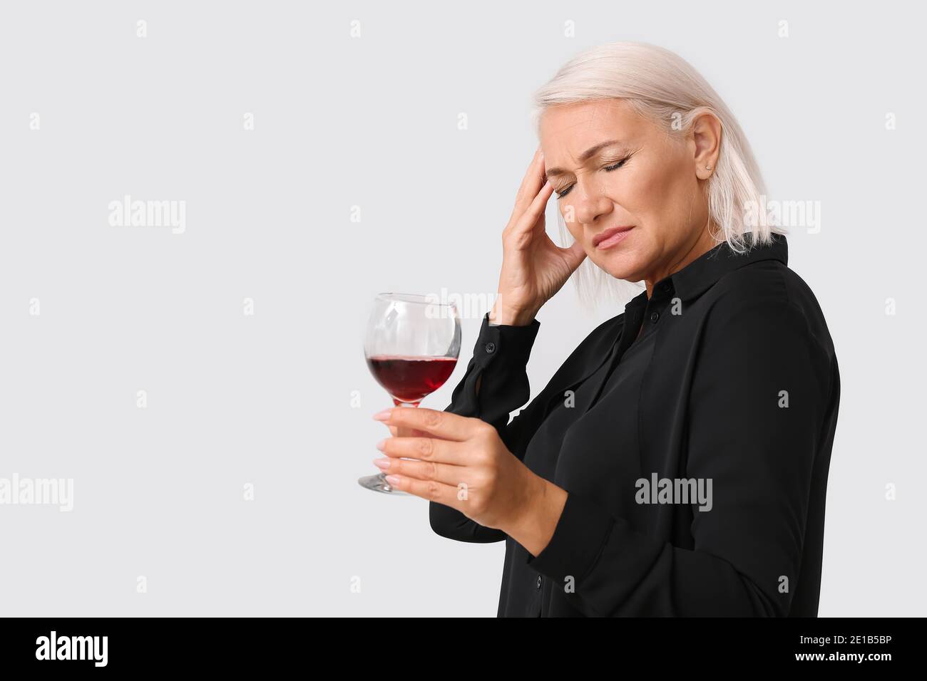 Stressed mature woman drinking wine on light background Stock Photo - Alamy