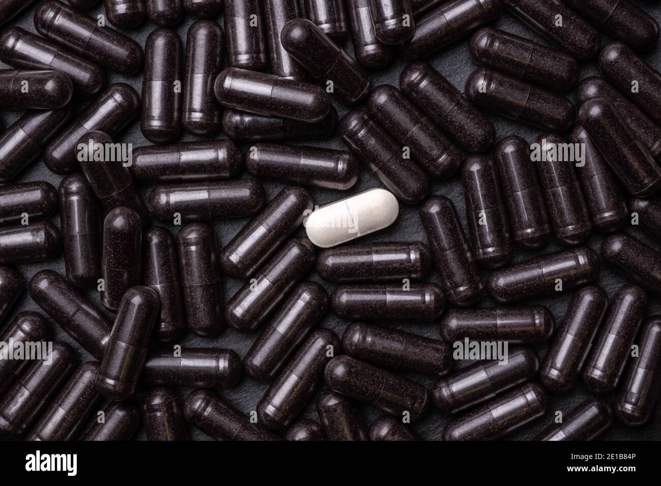 Medicine background from bunch of black pills and one white capsule in ...