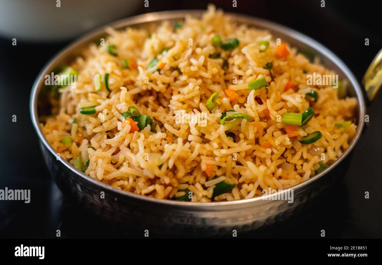A close up of Vegetable Fried Rice served in a wok pan on a black ...