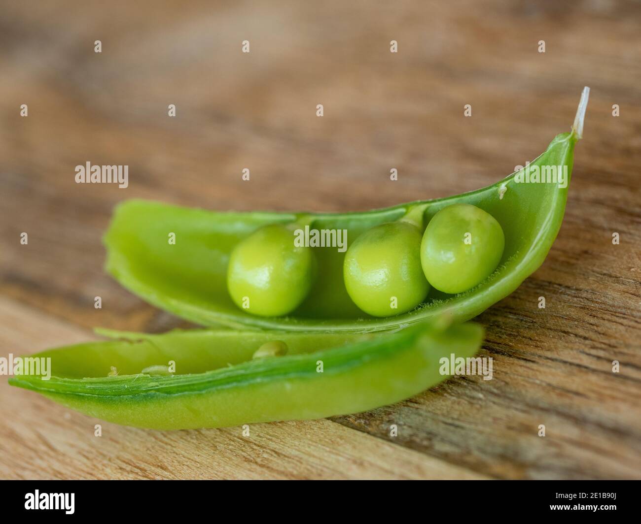 Vegetables, a trio of Green snap peas in an open pod on a wooden table ...