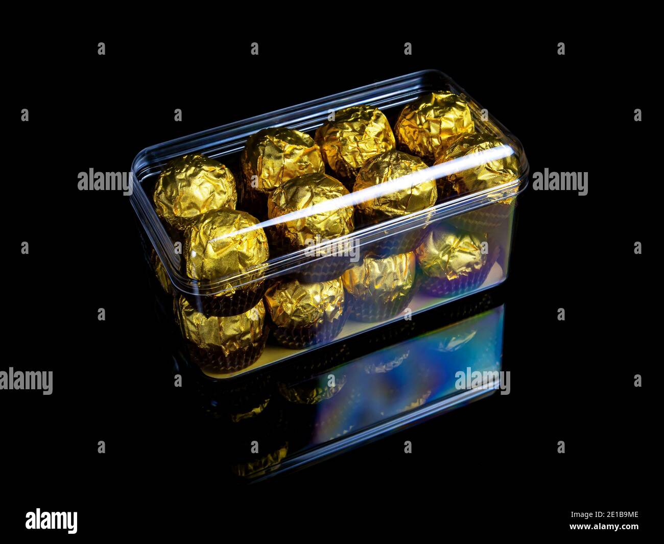 A box of round chocolates in a golden wrapper on a black background ...