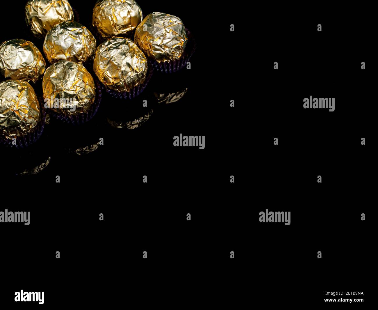 Round chocolate candies in a golden wrapper on a black background ...