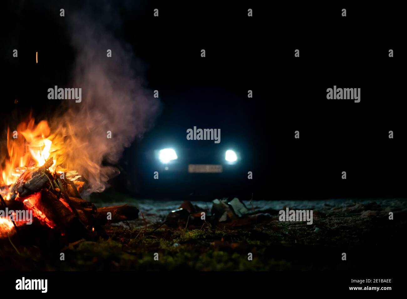 Beautiful bright bonfire at night, in the background a car with lights ...