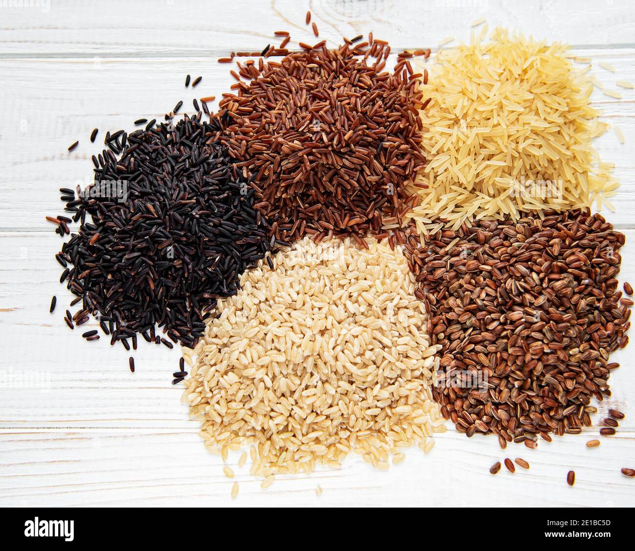 Set of various rice on white wooden background: black, basmati, brown ...