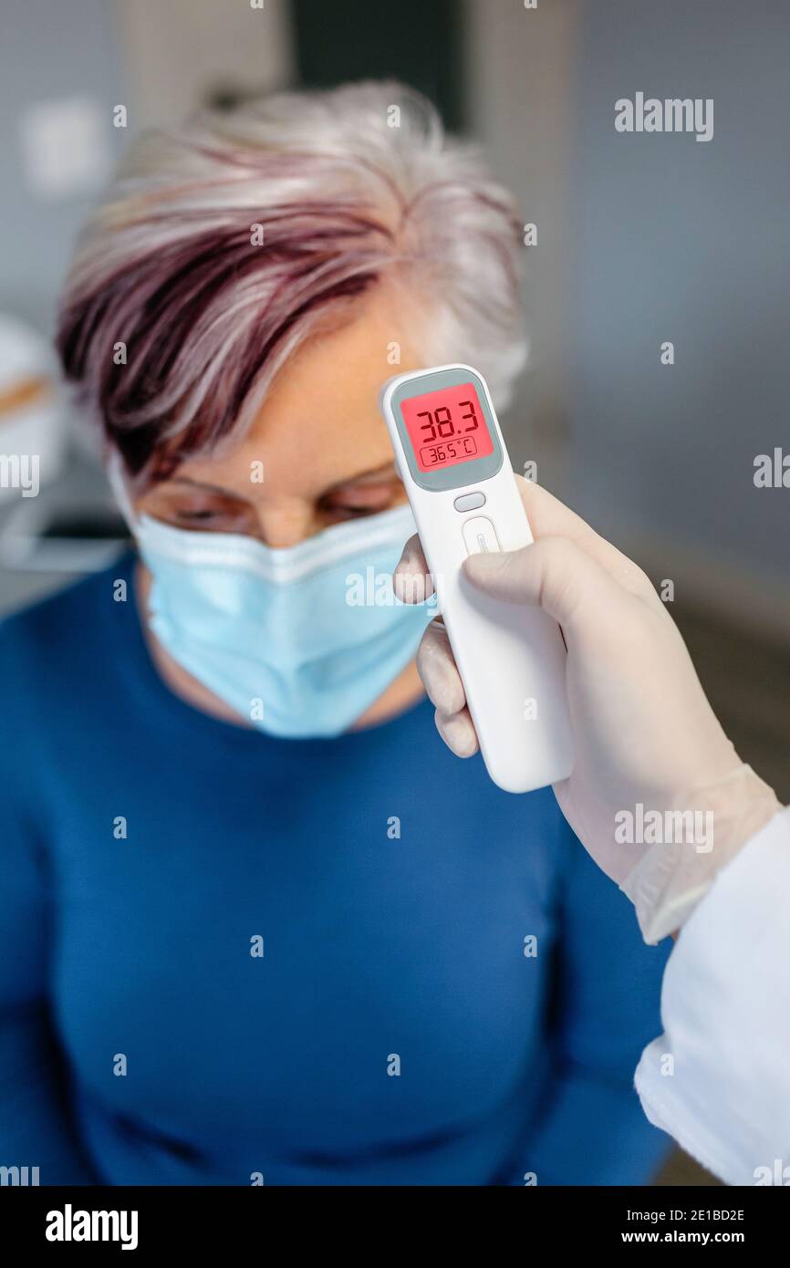 Senior woman with a fever whose temperature is taken by her doctor ...
