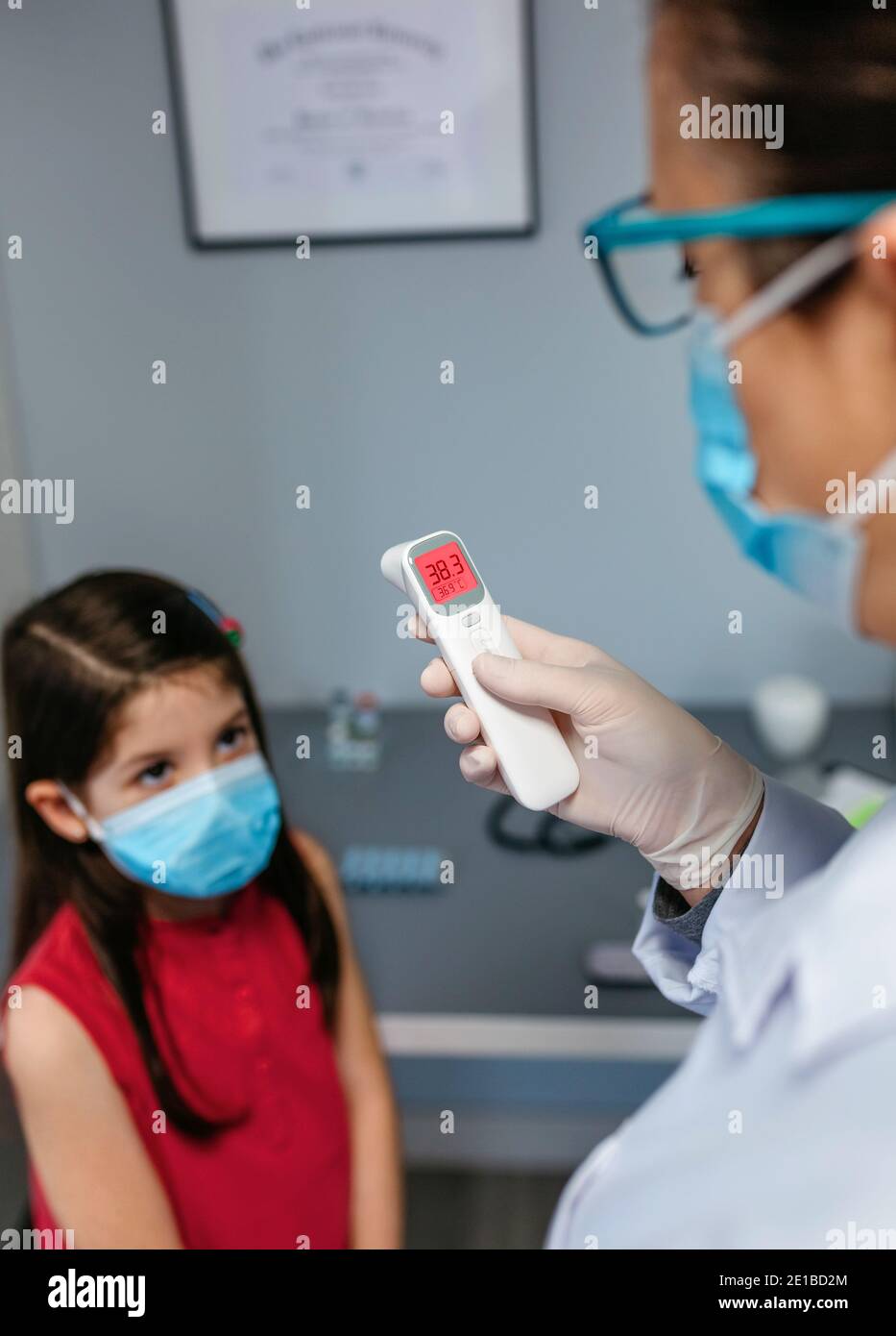 Female pediatrician looking at infrared thermometer after taking ...