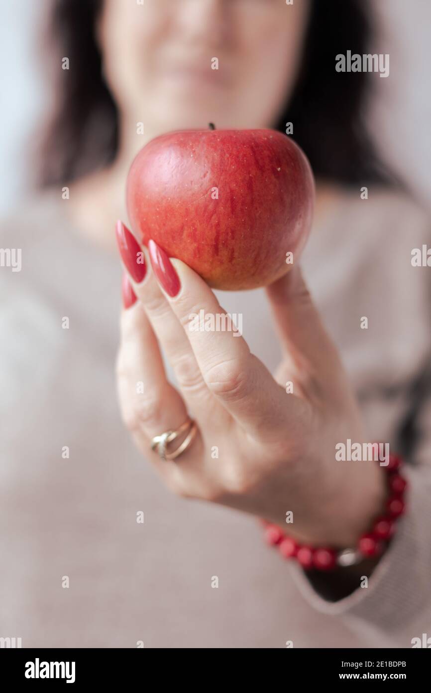 Female hands with red long nails are holding a ripe red apple fruit ...