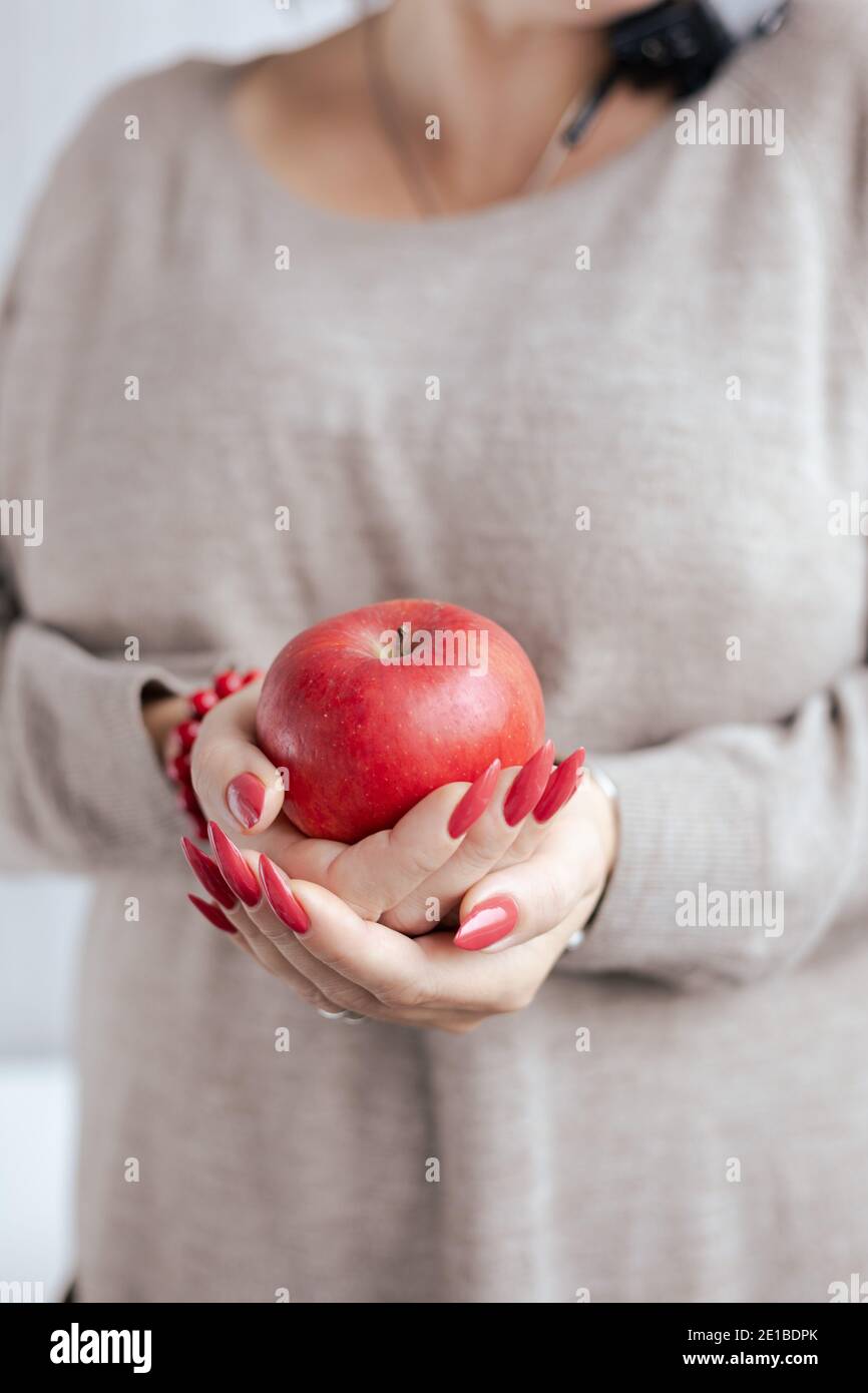 Female hands with red long nails are holding a ripe red apple fruit ...