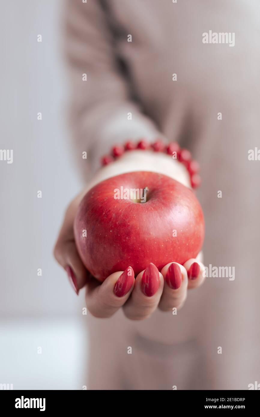 Female hands with red long nails are holding a ripe red apple fruit ...