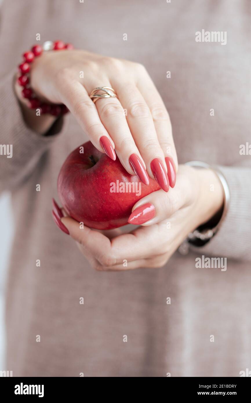 Female hands with red long nails are holding a ripe red apple fruit ...