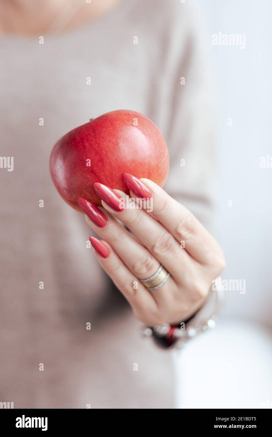 Female hands with red long nails are holding a ripe red apple fruit ...