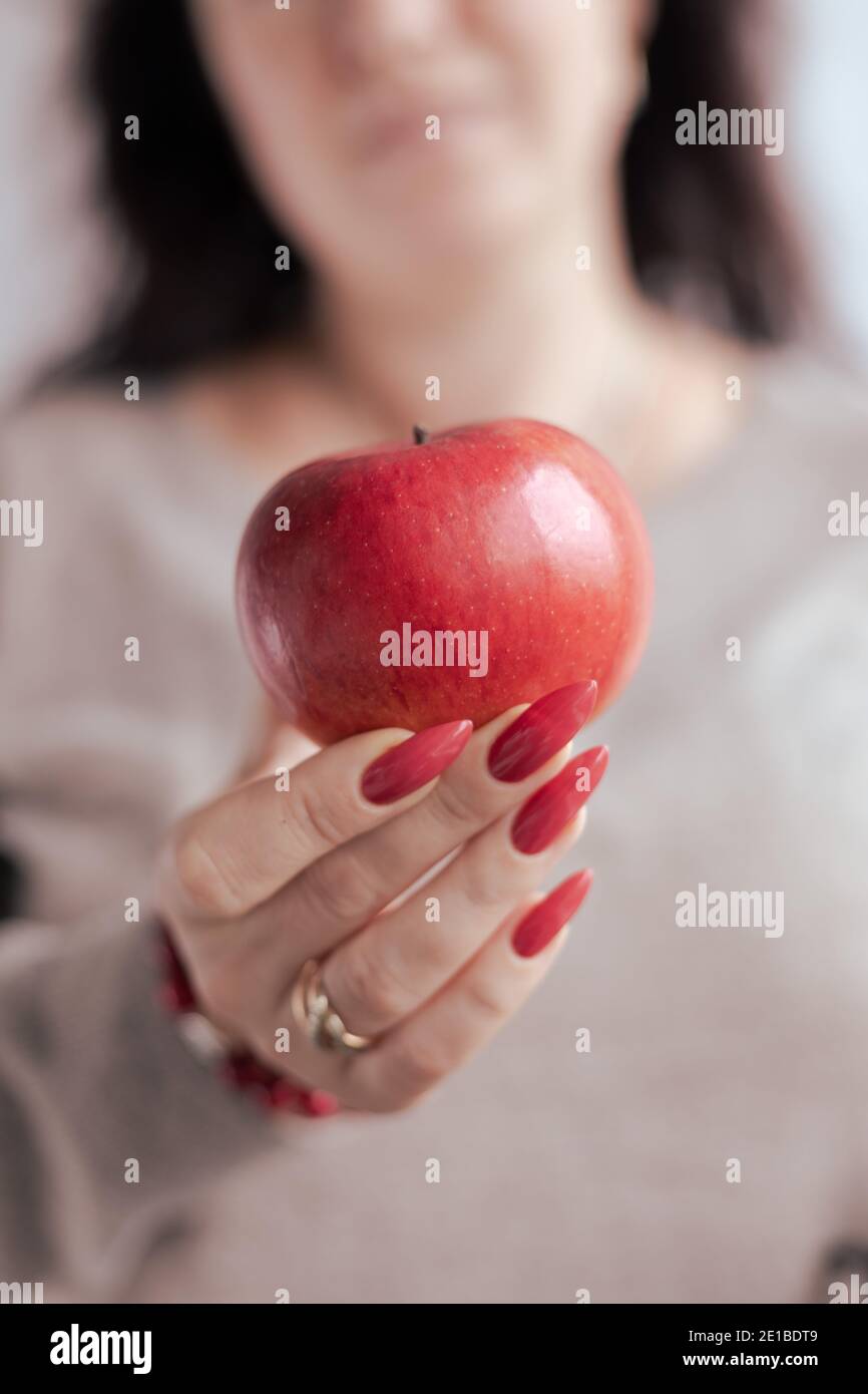 Female hands with red long nails are holding a ripe red apple fruit ...