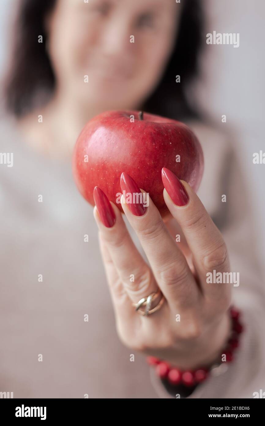 Female hands with red long nails are holding a ripe red apple fruit ...