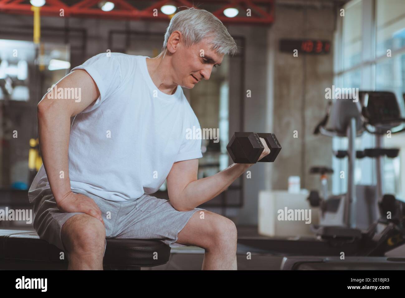 Strong healthy senior man doing biceps exercise with a dumbbell, copy ...