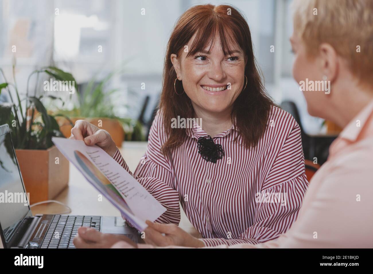 Lovely cheerful businesswoman smiling at her colleague, while doing ...