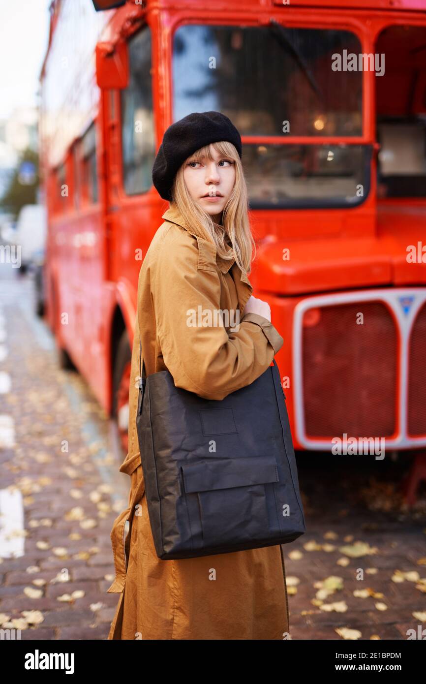 Blonde girl in black beret and trench on the city street background ...