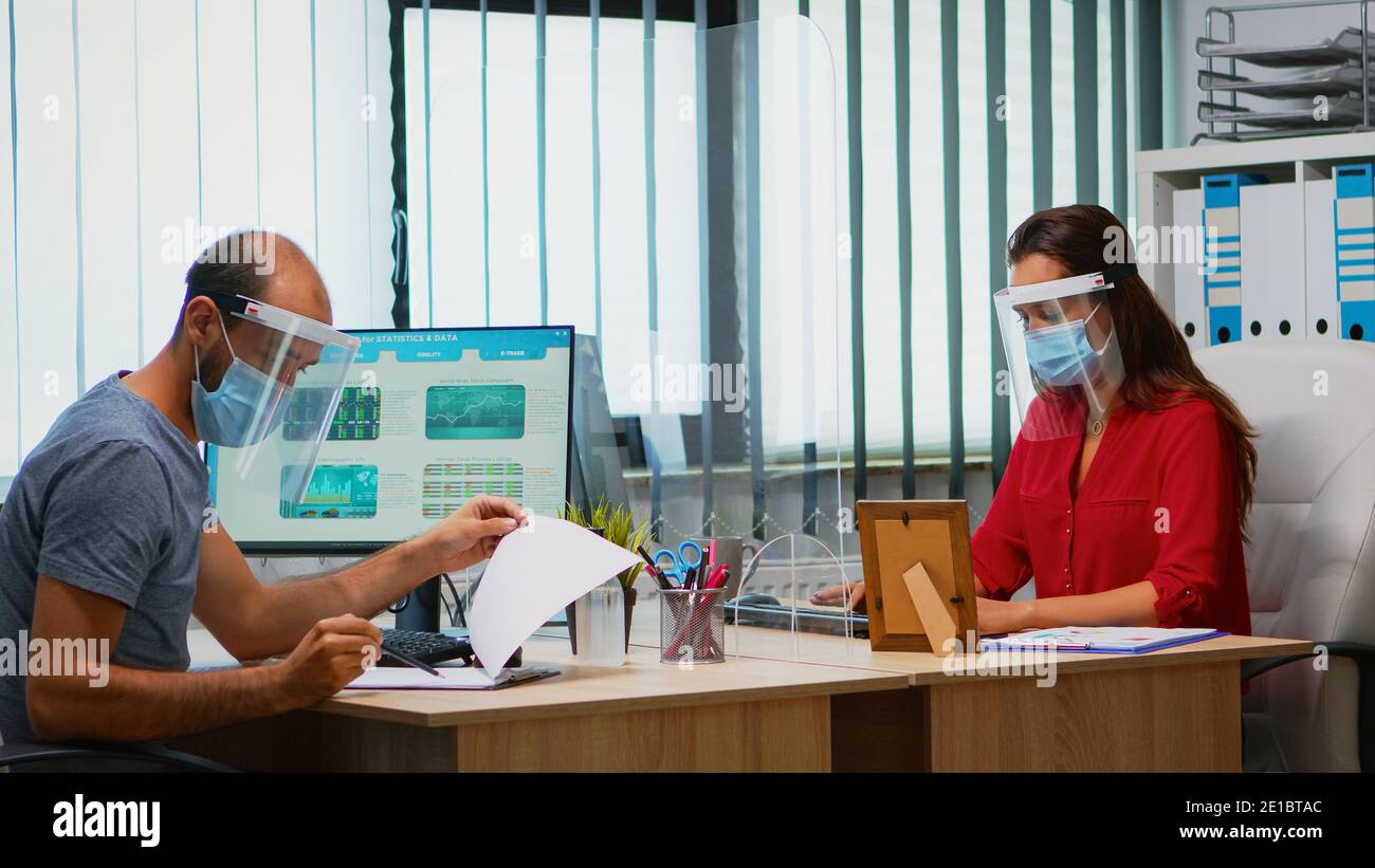 Employees wearing mask and visor sitting in new normal office room ...