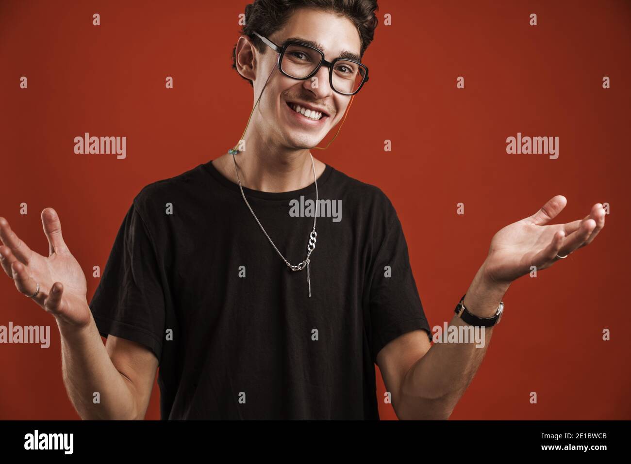 Confused smiling young hipster man standing isolated over red ...