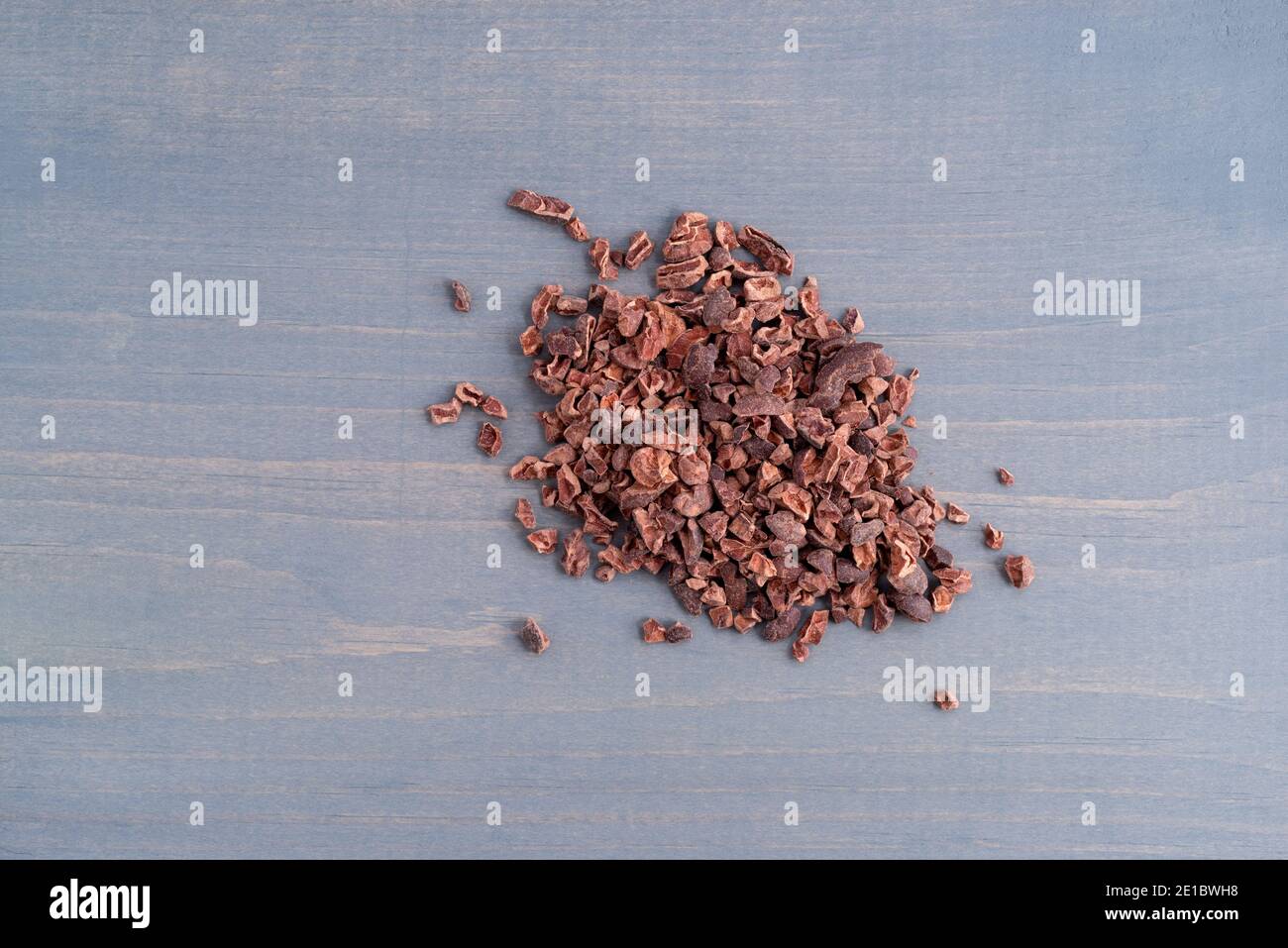 Small portion of cocoa nibs on a faded blue wood tabletop illuminated ...