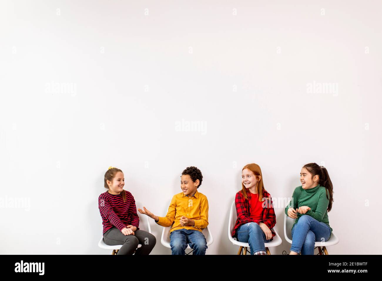 Portrait of cute little kids in jeans sitting in chairs against the ...