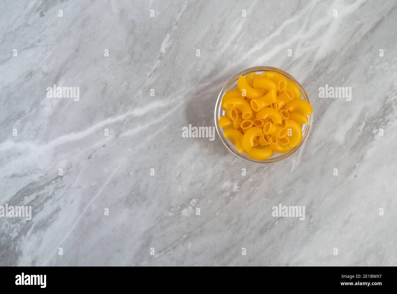 Organic elbow macaroni in a glass bowl offset on a gray countertop ...