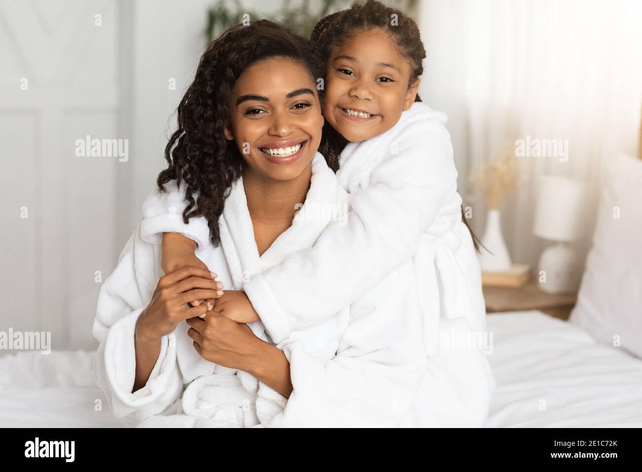 Beautiful Happy Black Mom And Daughter Posing On Bed In White Bathrobes Stock Photo - Alamy