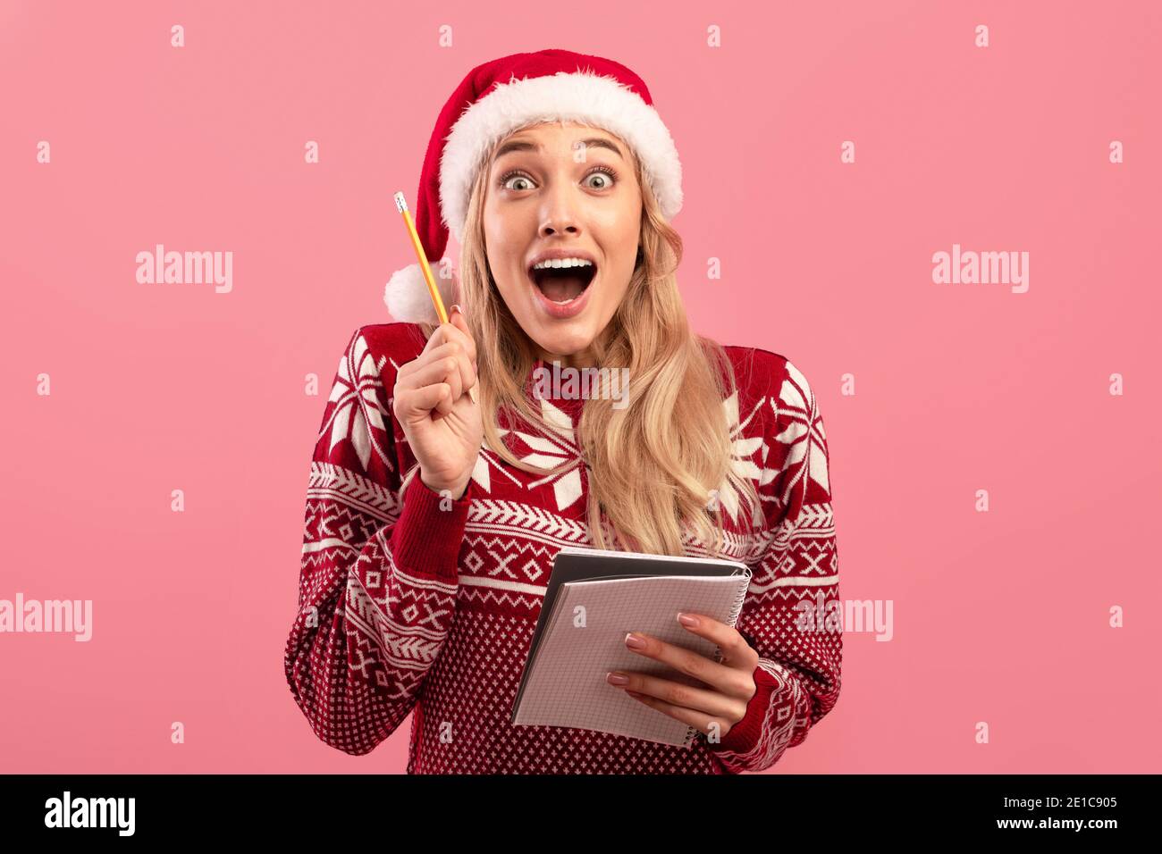 Excited young woman in Christmas sweater and Santa hat writing New Year ...
