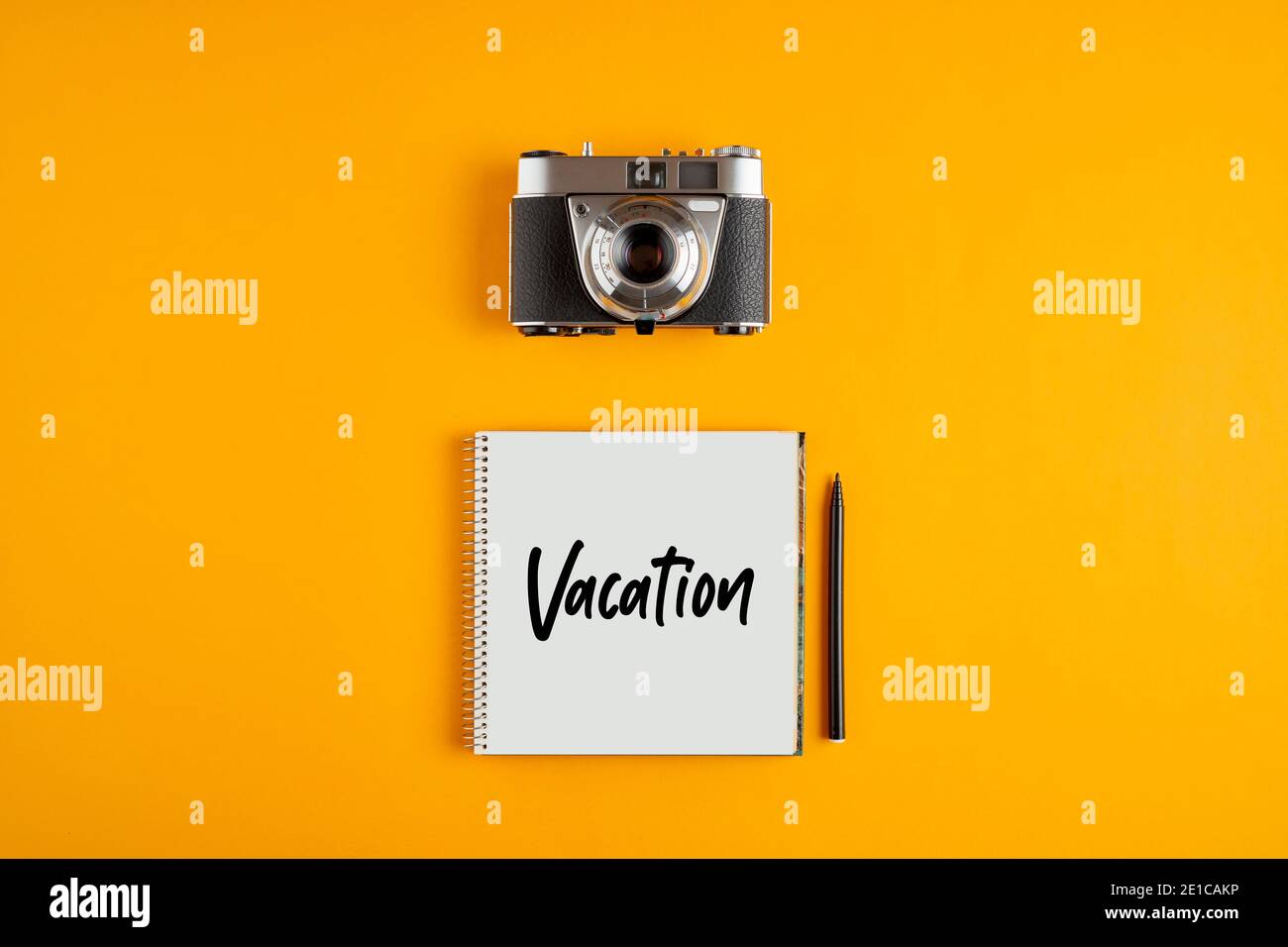Vintage camera with a notebook with the word vacation against yellow ...