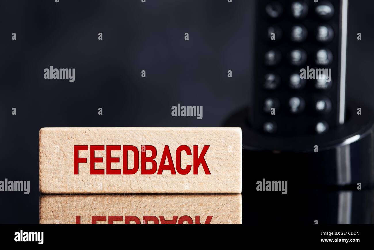 The word feedback on wooden block with phone against black background ...