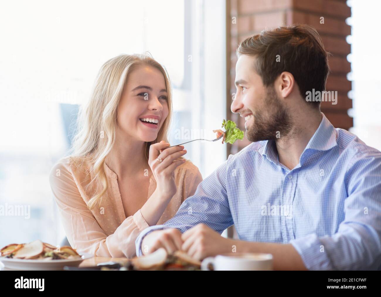 Cheerful millennial couple eating together at coffee shop, young lady ...
