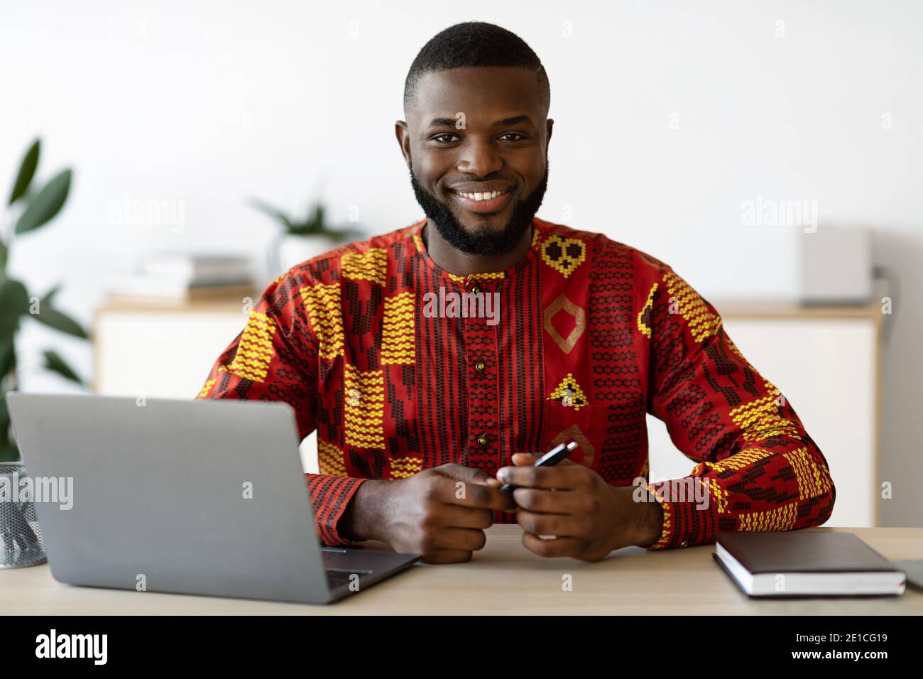 African Freelancer Guy In Traditional Costume Sitting At Desk At Home ...