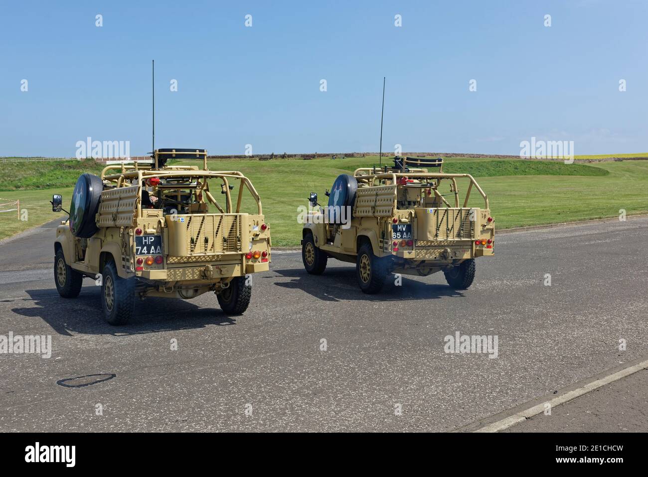 Two RWMIK Land Rovers waiting on a road facing a hill, as part of the ...