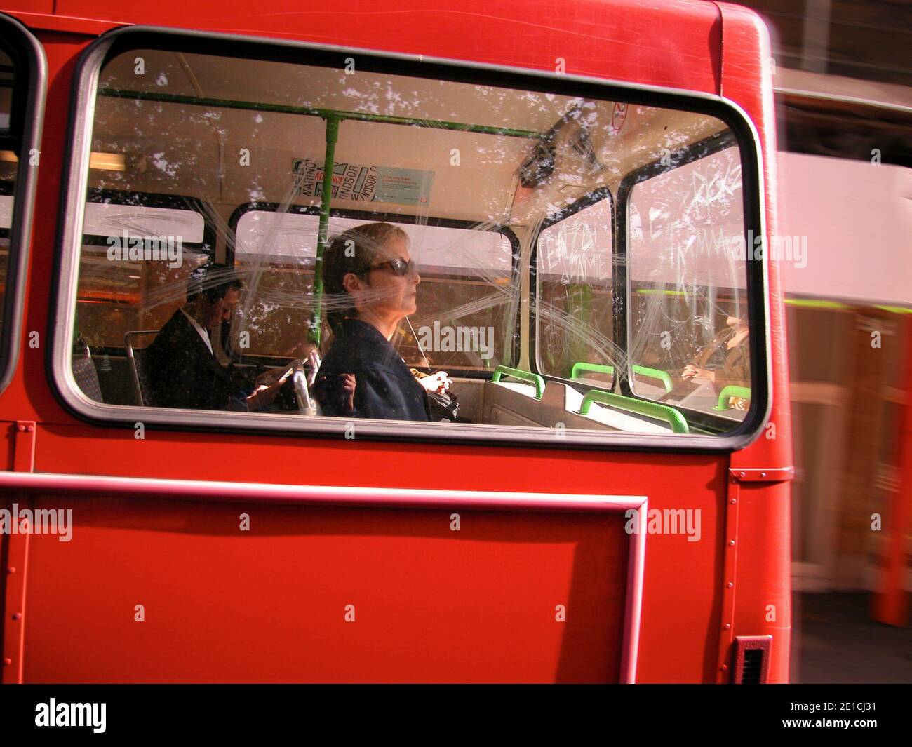 Bus passenger on red double decker bus, with scratched windows on top ...