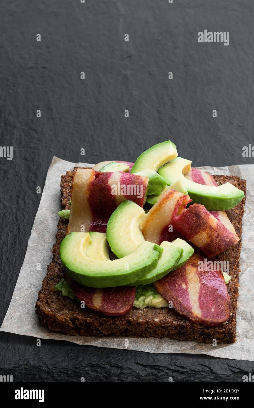 Sandwich with plant-based bacon rashers and avocado on black stone ...