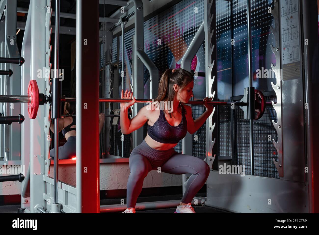 Beautiful young fitness woman doing squats with a barbell on the Smith ...