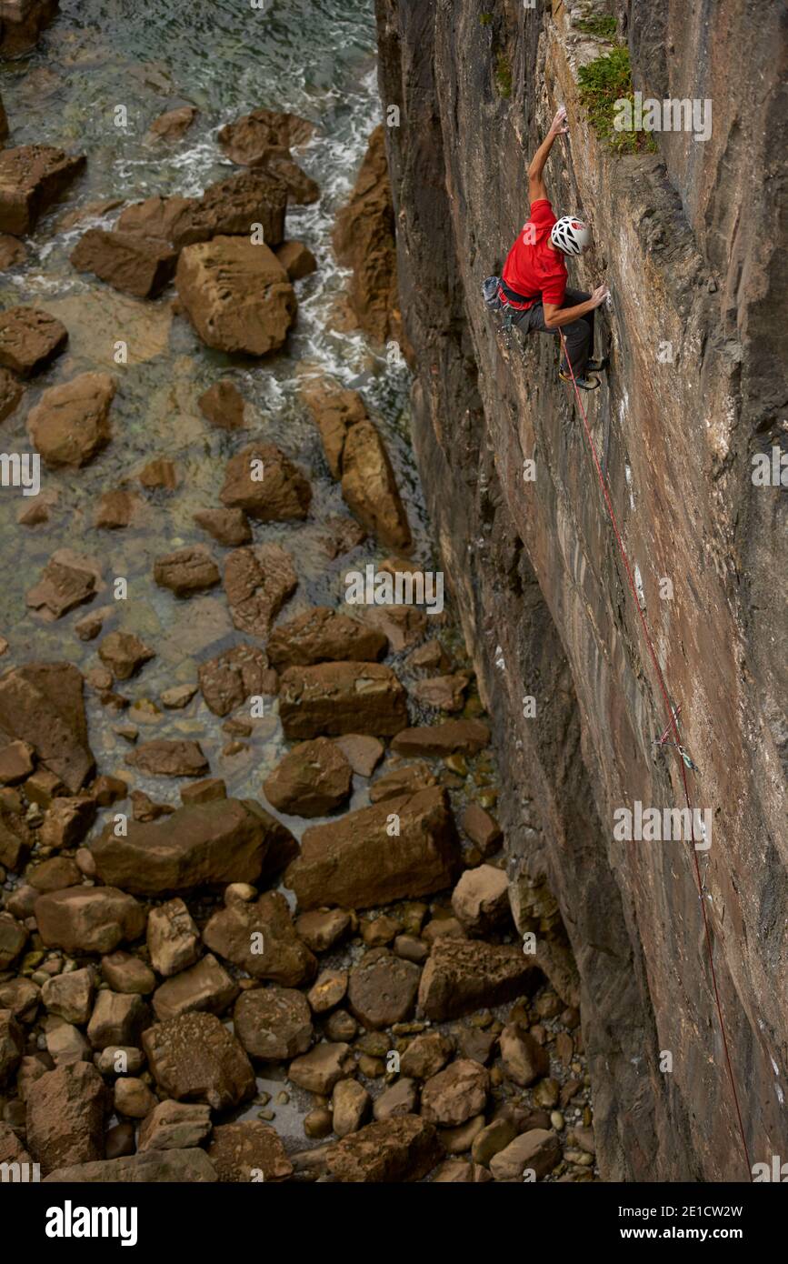 High angle view shot of an adventurous man rock climbing up a cliff ...