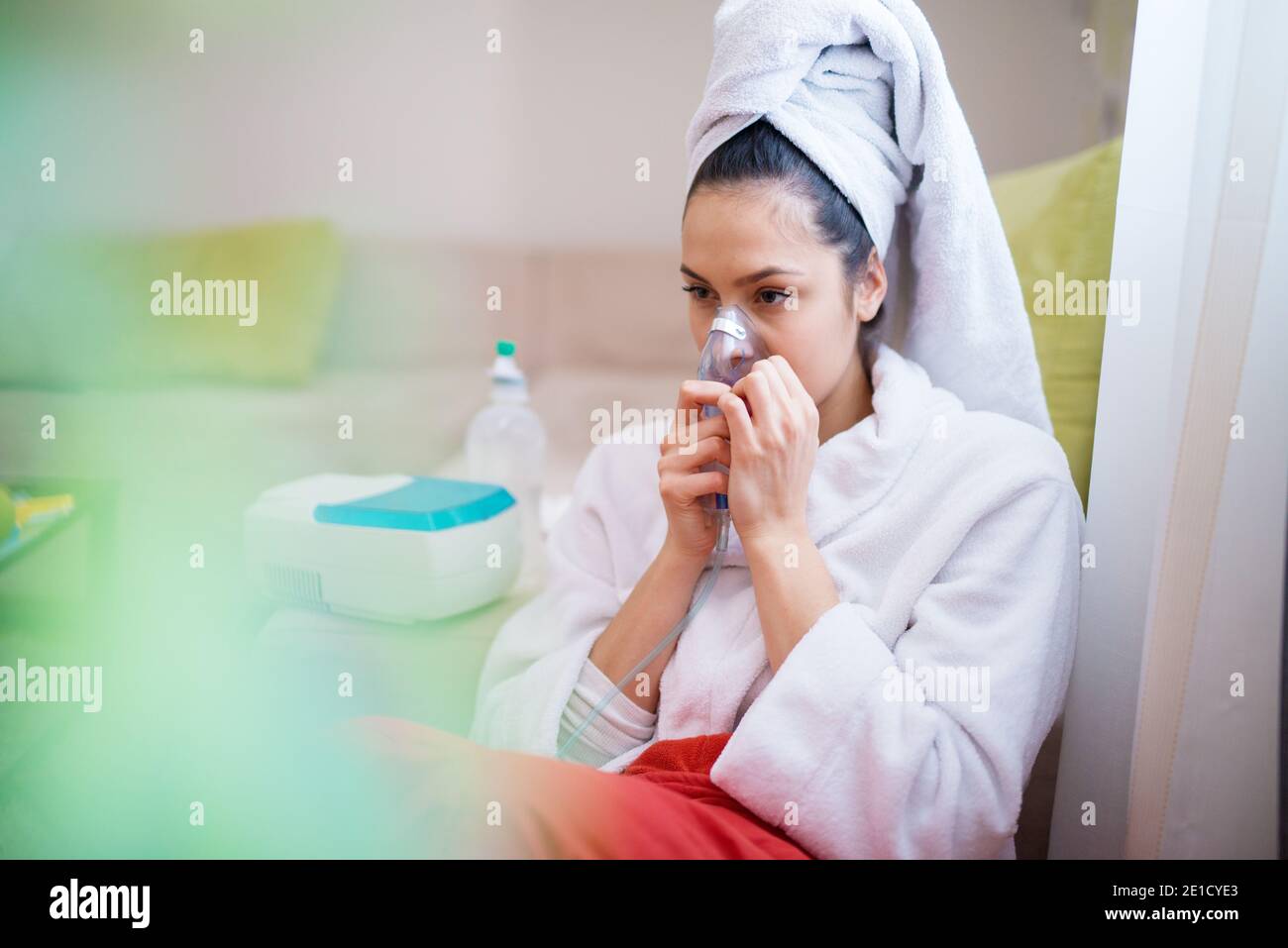 Young beautiful and exhausted female is using the inhaler on her sofa ...