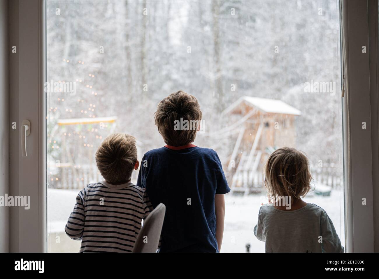 Three kids, siblings, looking out the window at a beautiful snowy ...