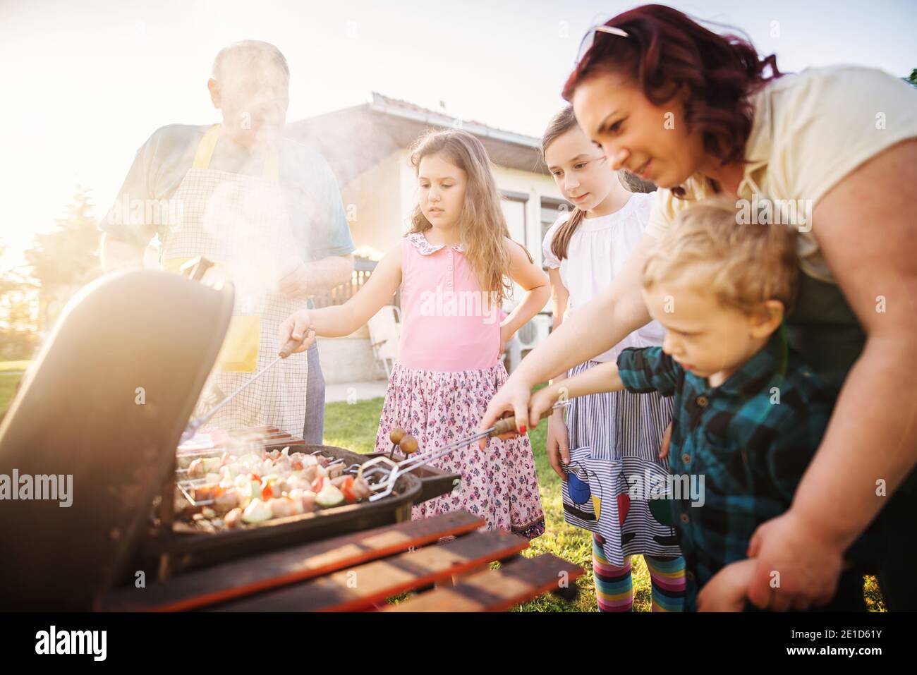 Proud mother of tree children is showing them how to make some barbeque ...