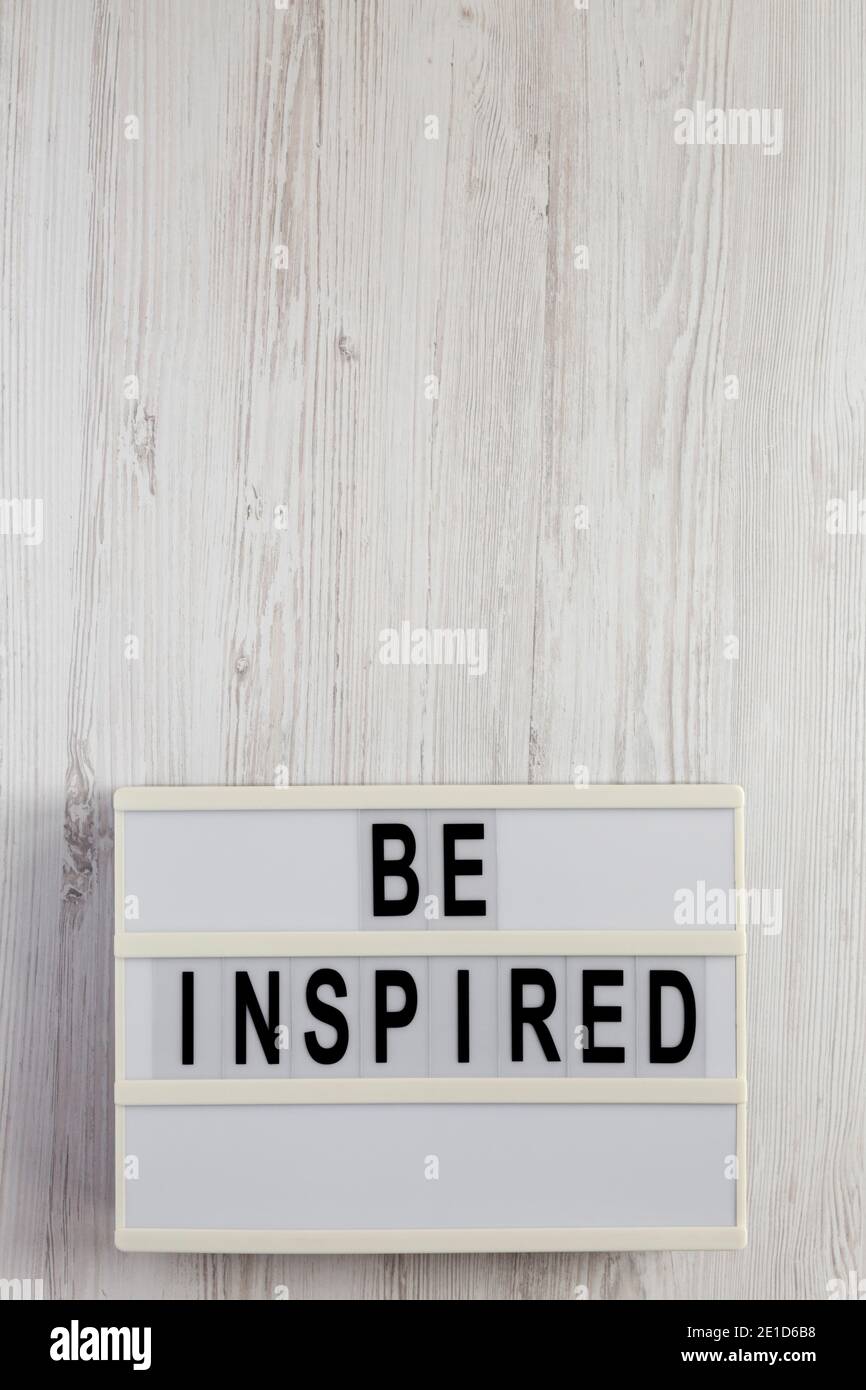 'Be inspired' on a lightbox on a white wooden background, overhead view ...