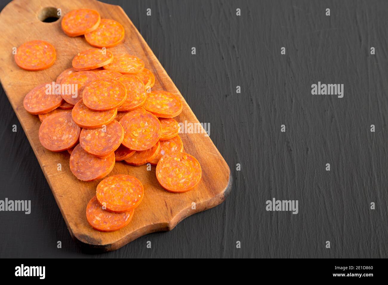 Italian Pepperoni Slices on a rustic wooden board on a black background ...